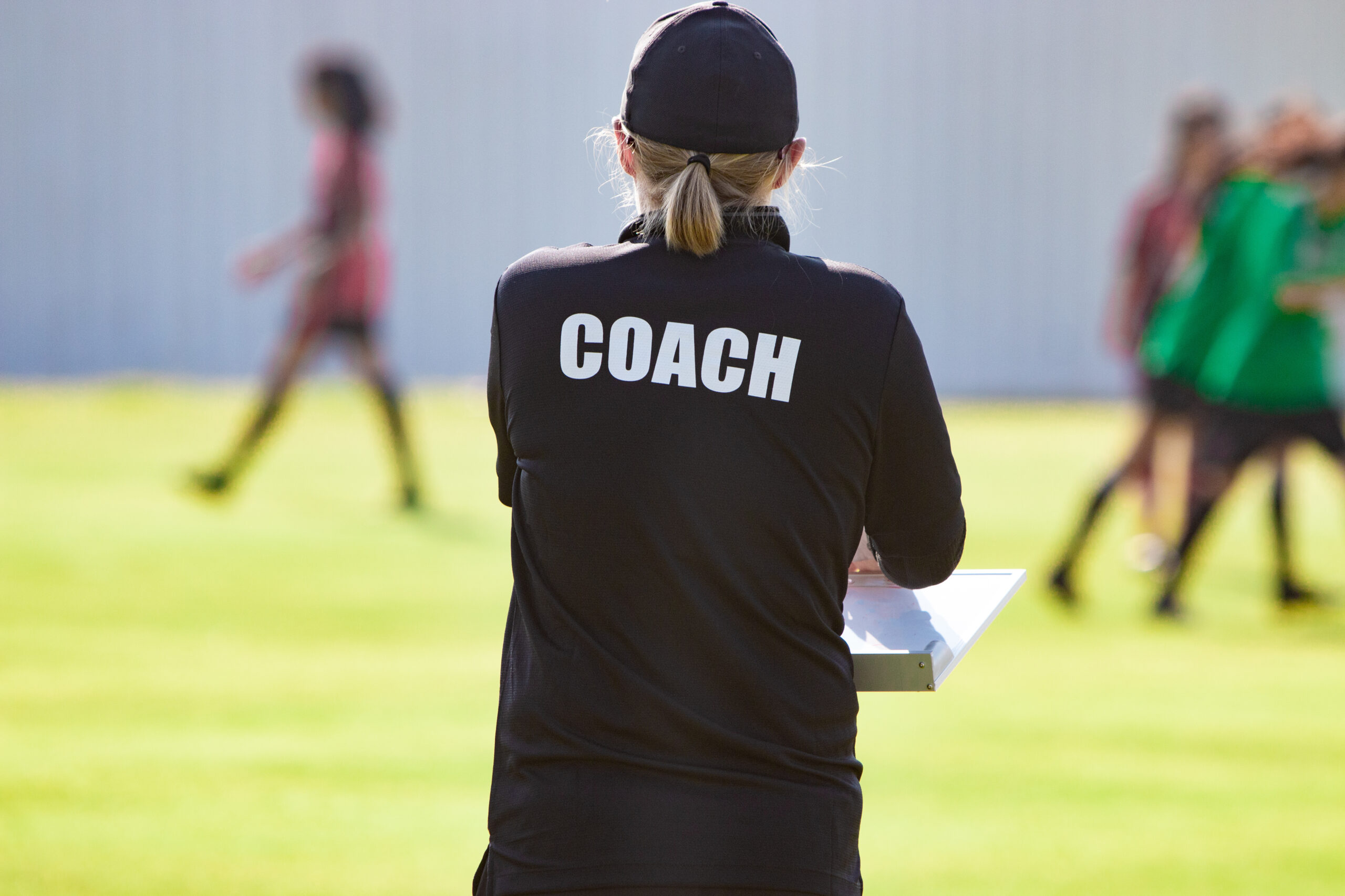 Back view of female football coach in black COACH shirt at an outdoor ...